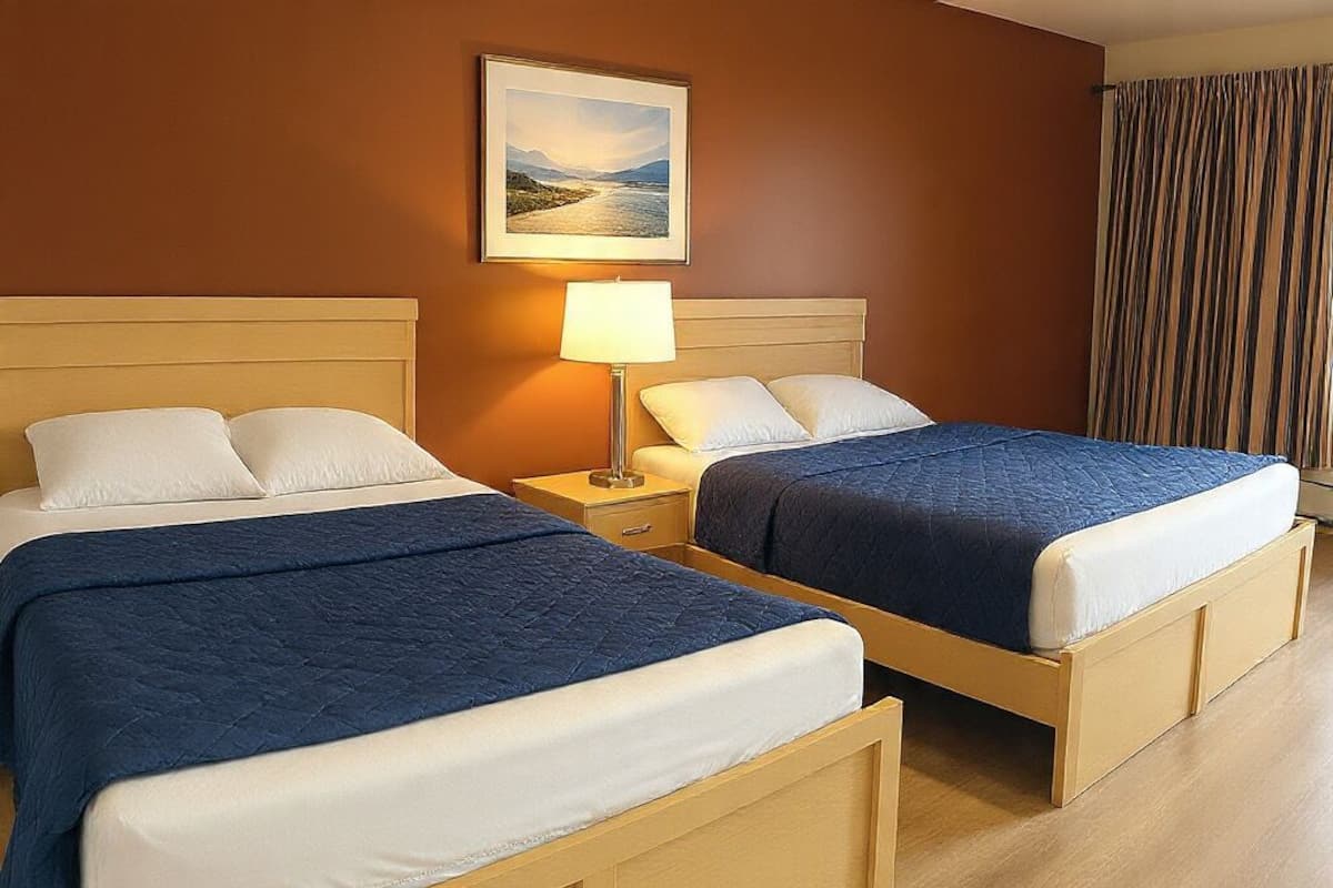 Quarto de hotel com duas camas, uma mesa de cabeceira, uma luminária e um quadro na parede.