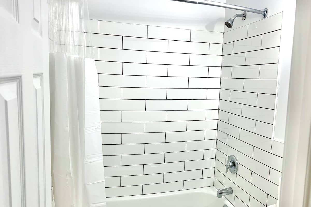 Casa de banho com paredes de azulejos tipo metrô brancos, uma banheira branca e um chuveiro com porta de vidro.