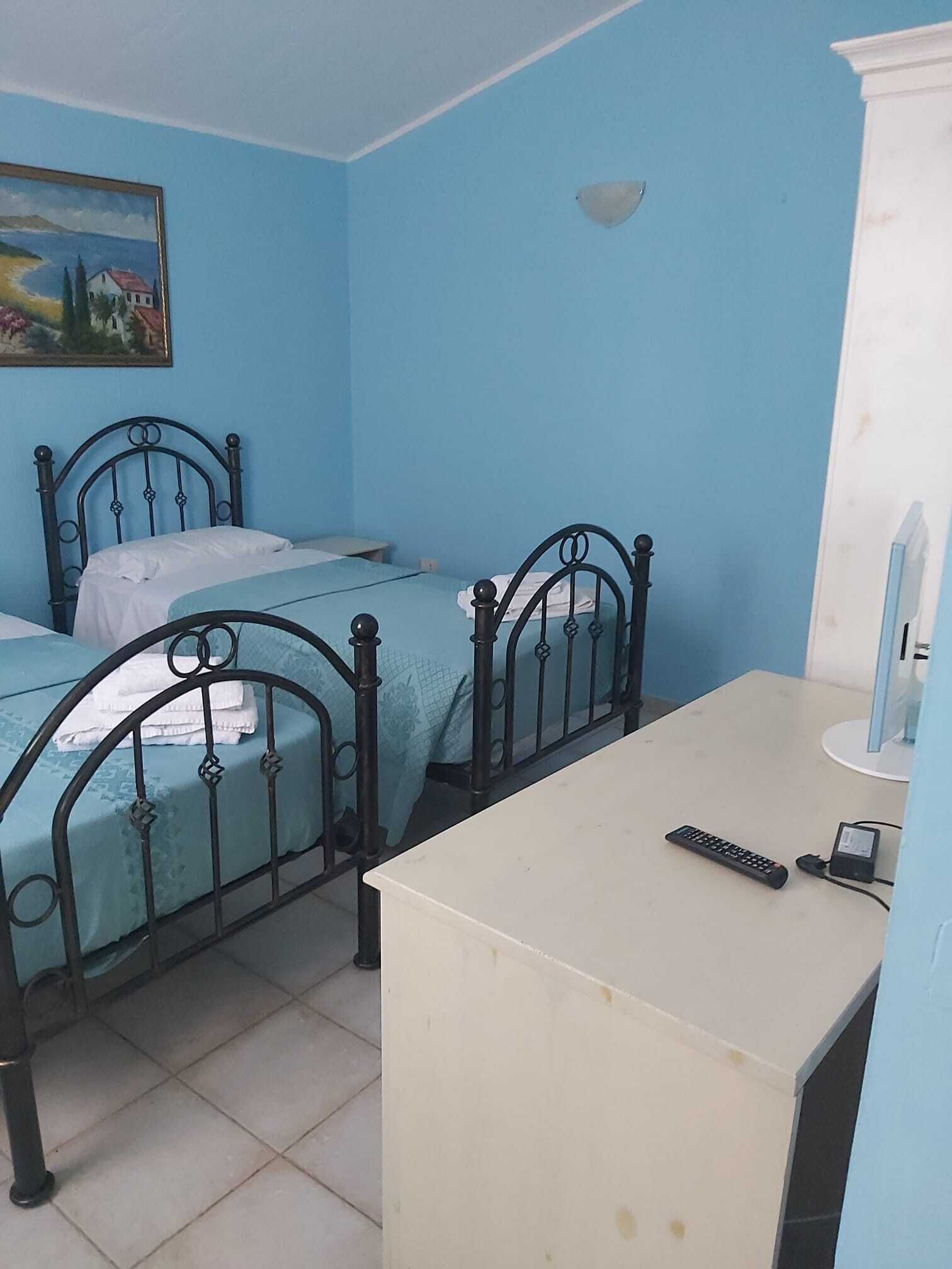 Quarto com duas camas, uma escrivaninha e um quadro na parede.