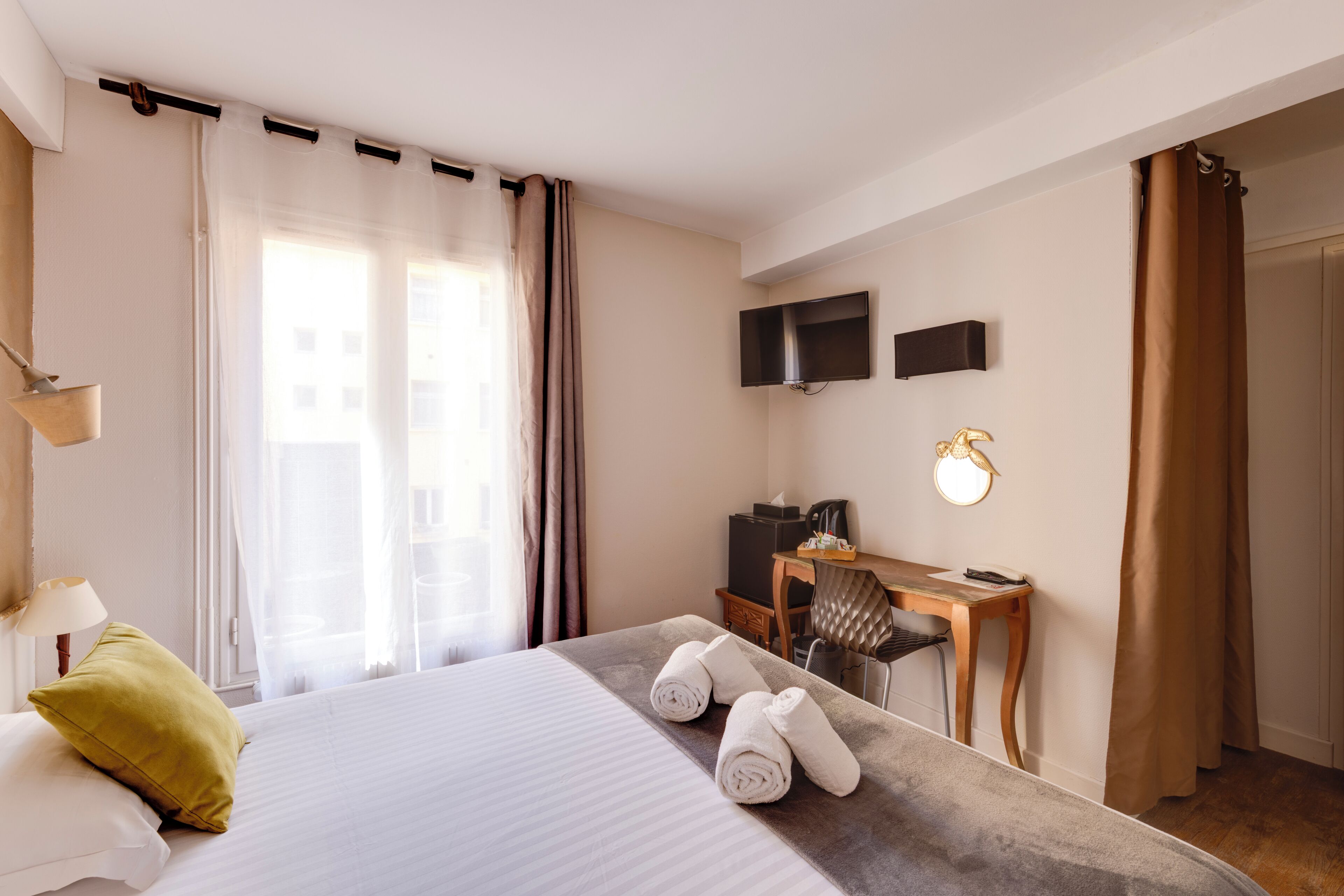 Quarto de hotel com cama, escrivaninha, televisão e janela com cortinas.