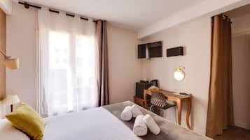 Quarto de hotel com cama, escrivaninha, televisão e janela com cortinas.