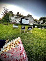 Espaço para exibição de filmes ao ar livre, com uma tela grande, várias áreas de estar e uma mesa de lanches com pipoca.