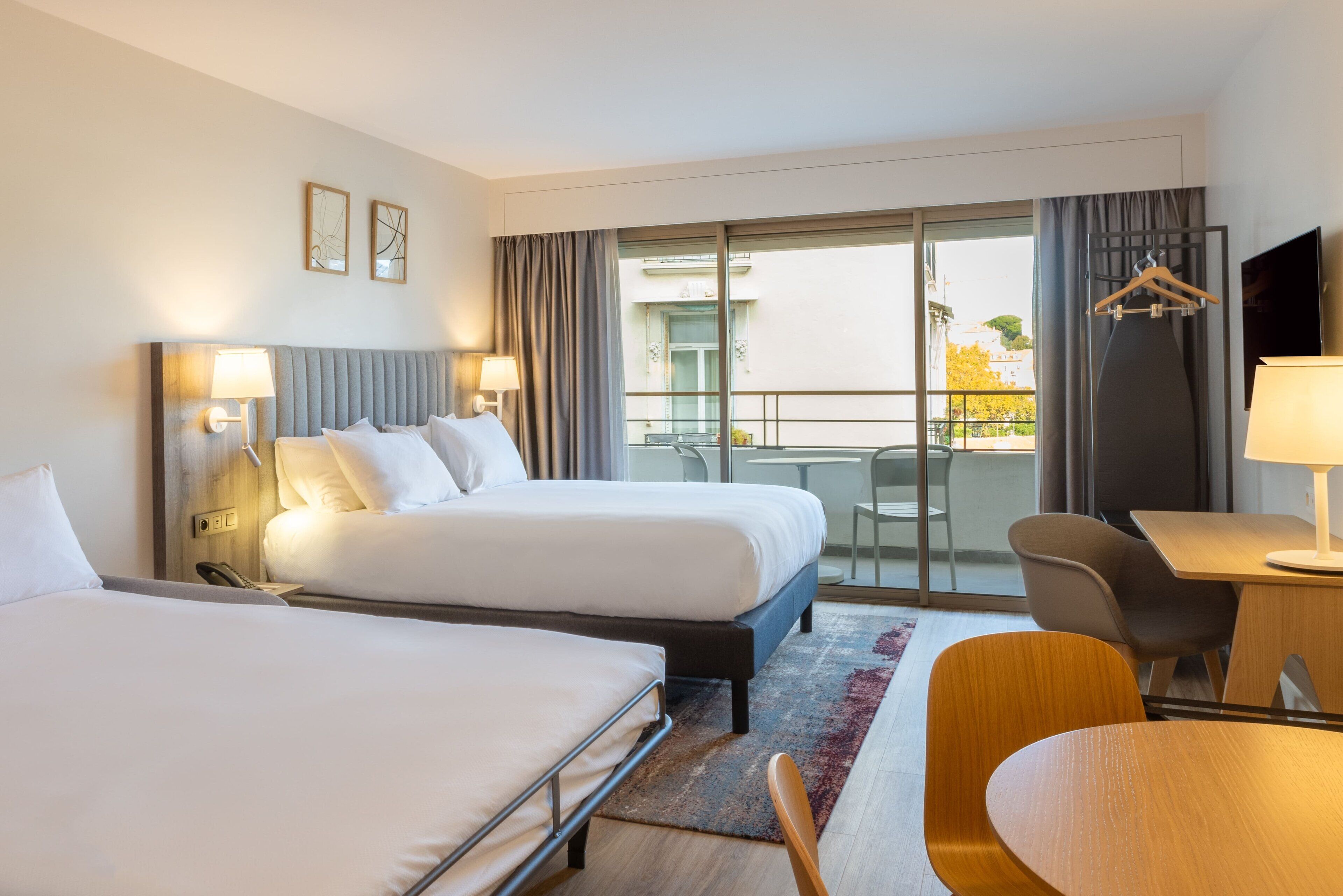 Quarto de hotel com duas camas, uma escrivaninha, uma cadeira e varanda com vista.
