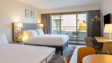 Quarto de hotel com duas camas, uma escrivaninha, uma cadeira e varanda com vista.