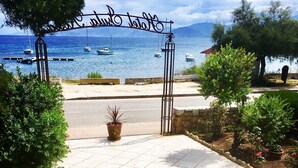 Uma área de entrada pavimentada com um letreiro, plantas em vasos e vista para o mar com barcos.