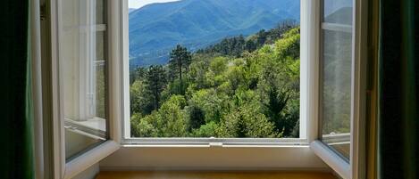 Quarto com escrivaninha e cadeira de madeira, janela com vista para uma paisagem montanhosa.