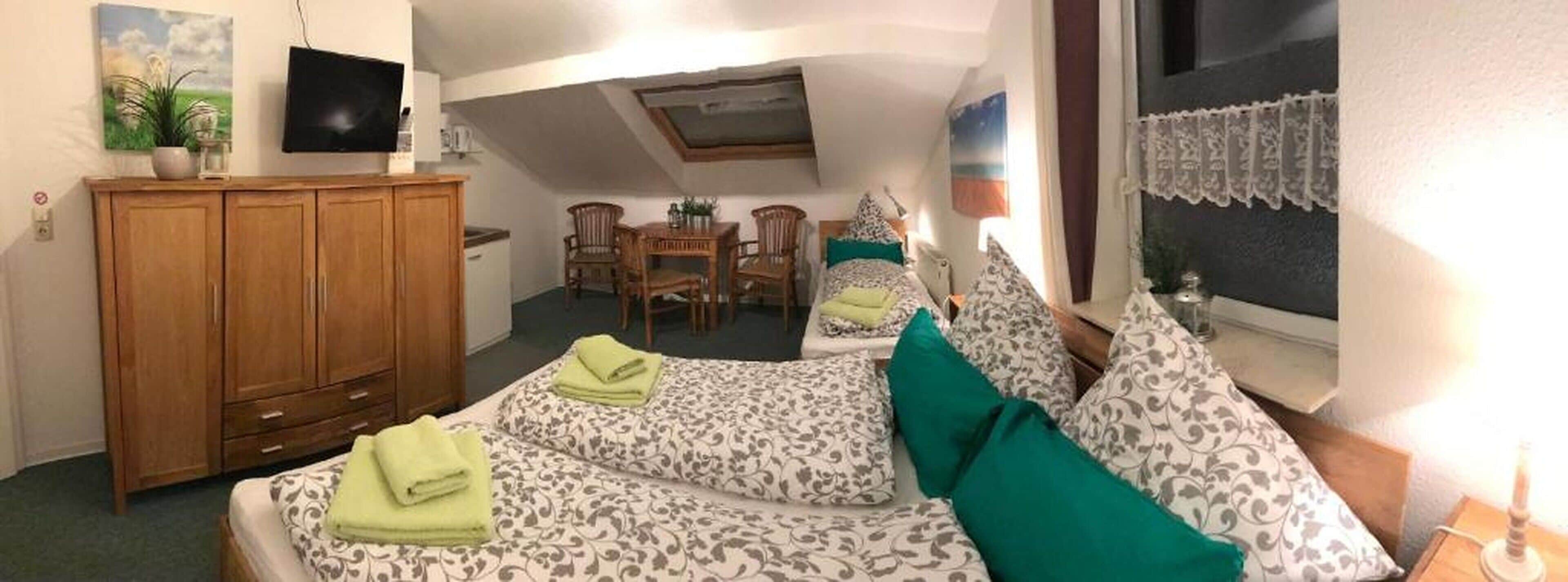 Quarto aconchegante com uma cama, um guarda-roupa de madeira, uma mesa de jantar com cadeiras e uma TV na parede.