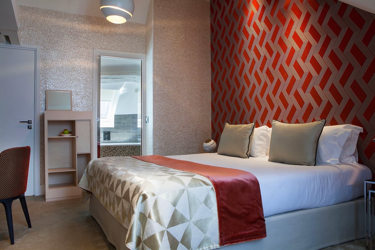 Quarto de hotel com cama, uma cadeira, guarda-roupa e parede estampada.