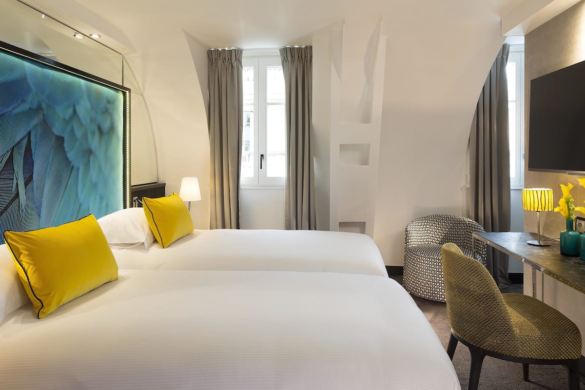 Quarto de hotel com duas camas, uma escrivaninha, uma cadeira, uma televisão e janela com cortinas.