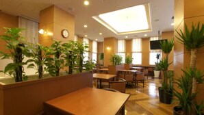 Um saguão de hotel com mobiliário de madeira, plantas em vasos, um relógio e uma televisão de tela plana.