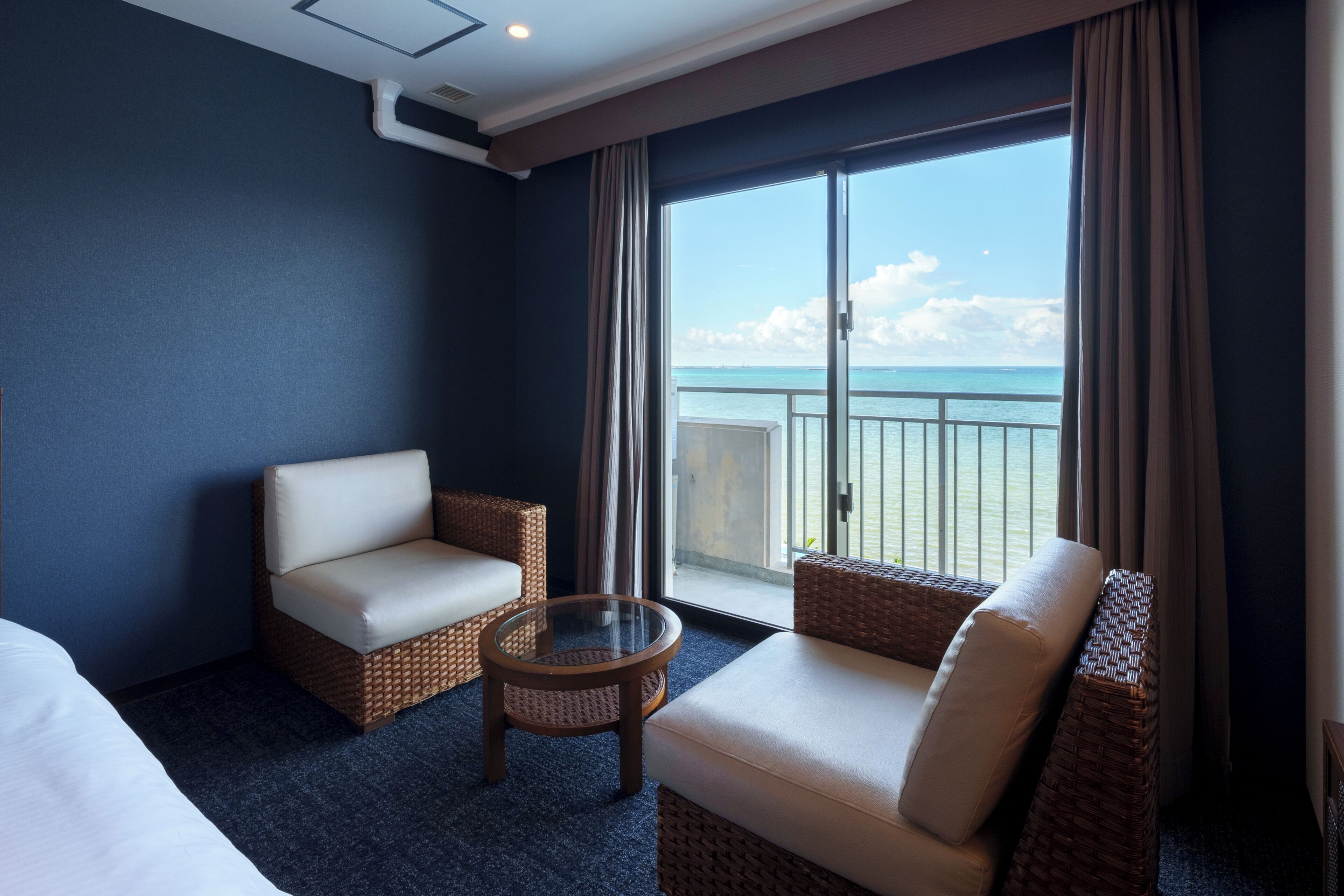 Quarto de hotel com varanda, dois sofás, uma mesa pequena e uma cama.