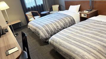 Quarto de hotel com duas camas, uma escrivaninha, uma cadeira, uma mesinha e um abajur.