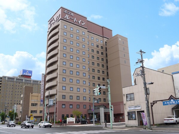 Um hotel com vários andares, um letreiro chamativo, diversas janelas e um cruzamento movimentado com carros e semáforos.