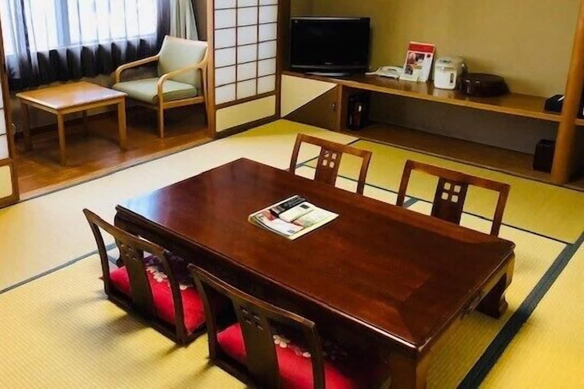 Quarto japonês tradicional com tatames, uma mesa baixa com cadeiras, uma televisão e uma estante com objetos.