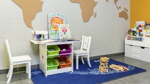 Uma área de recreação infantil com uma mesa branca, caixas de armazenamento coloridas e um mapa-múndi na parede.