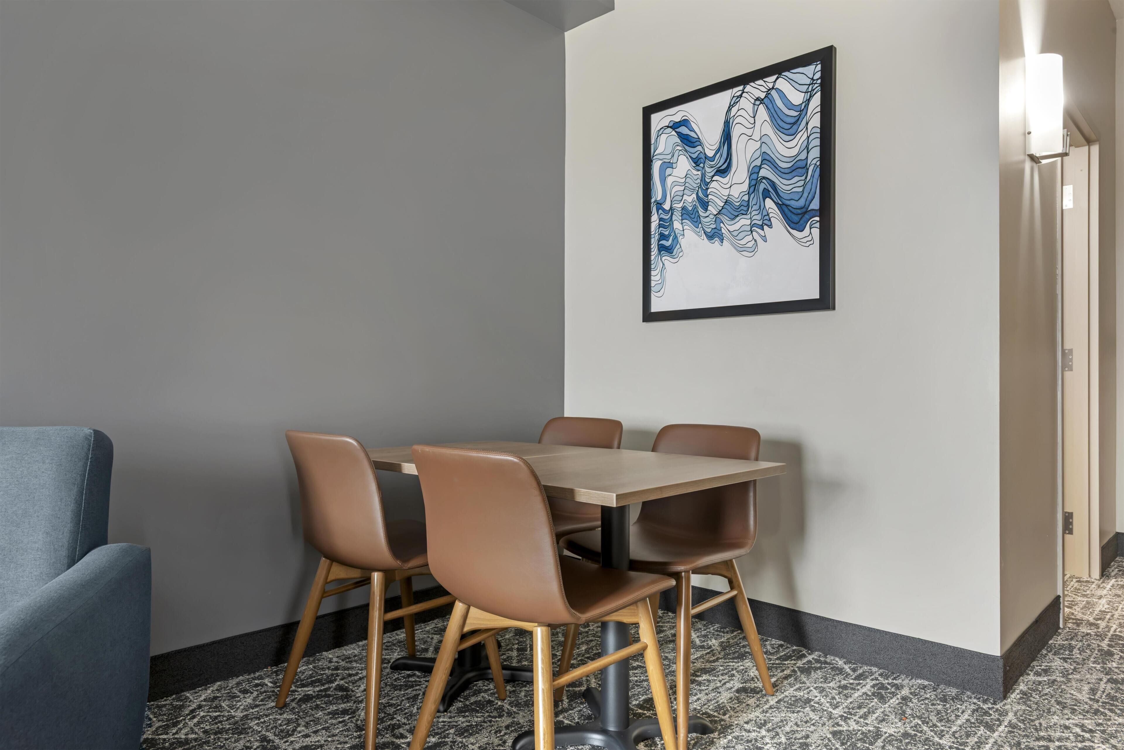Uma sala de conferência com mesa e cadeiras, uma obra de arte abstrata emoldurada na parede e piso coberto de carpete.