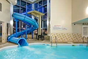 Piscina interna com escorregador azul e placa indicando 'proibido mergulhar'.