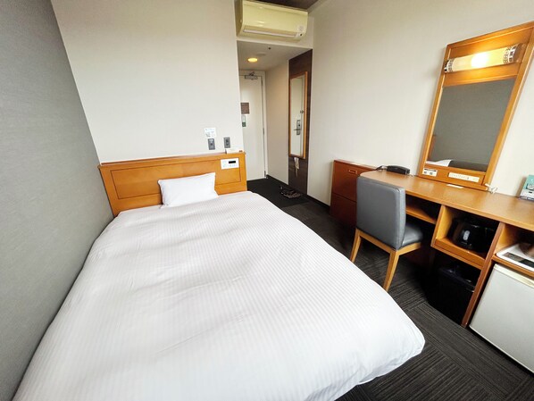 Quarto de hotel com cama, escrivaninha, cadeira, espelho e um pequeno armário.