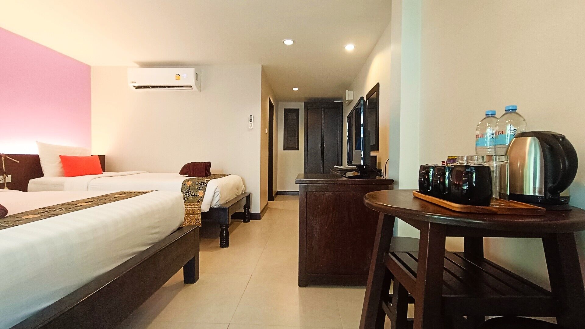 Quarto de hotel com duas camas, uma escrivaninha com chaleira e televisão.