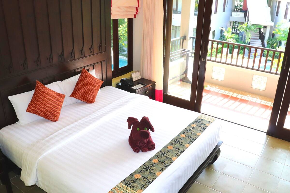 Quarto de hotel com cama, almofadas, mesa de cabeceira e vista para a varanda.