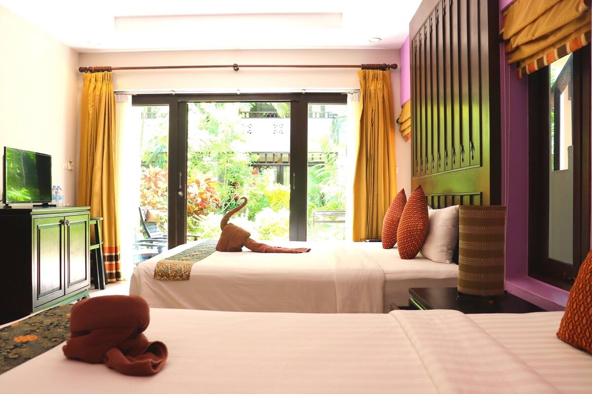 Quarto de hotel com duas camas, televisão e vista para um jardim através de uma porta de correr.