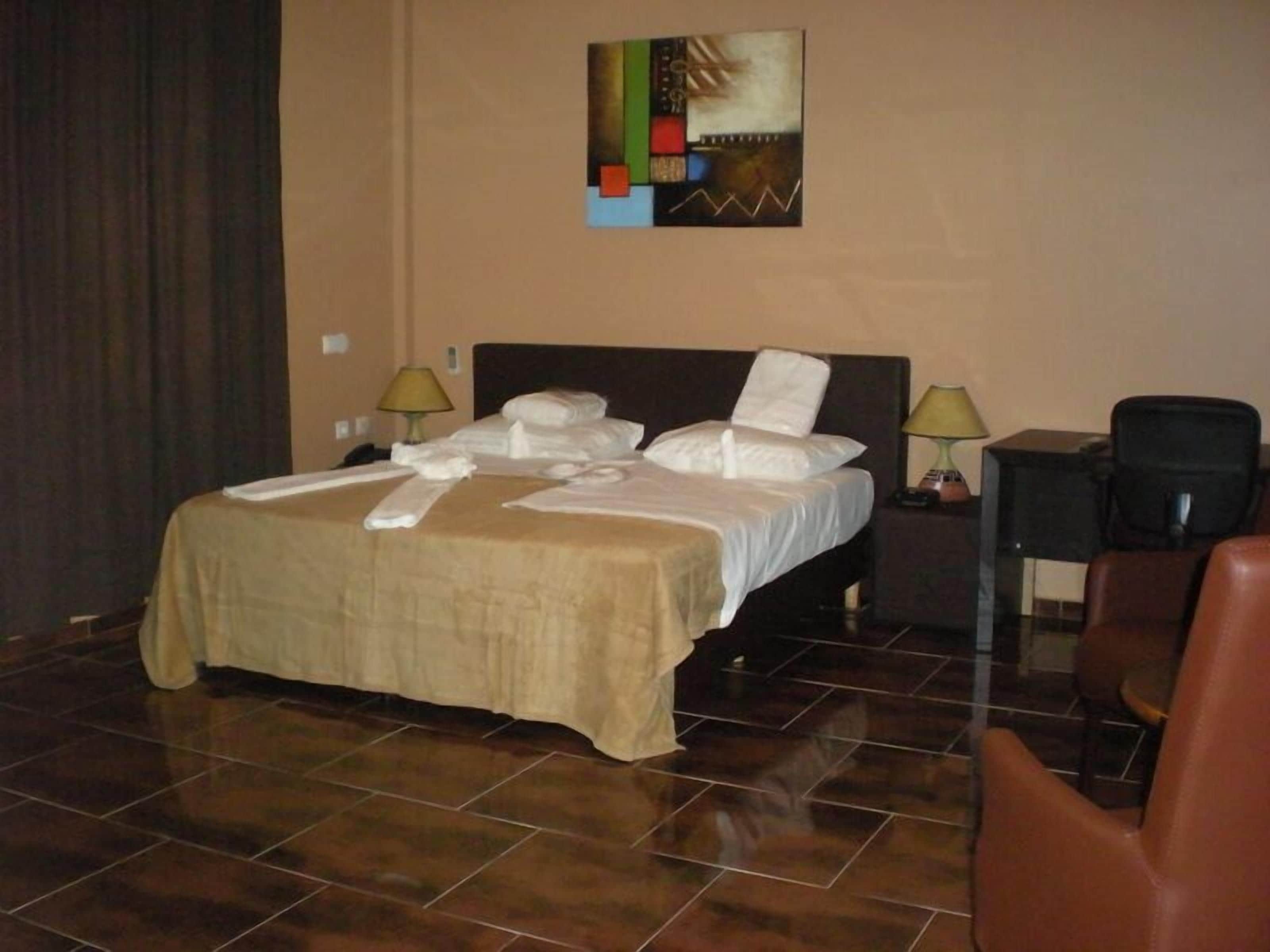 Quarto de hotel com cama, duas luminárias de cabeceira, uma mesa e uma cadeira.