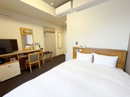 Quarto de hotel com cama, escrivaninha com cadeira, televisão e espelho.
