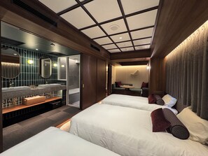 Quarto de hotel com uma cama grande, área de estar separada, toucador com espelhos e teto com padrão quadriculado.