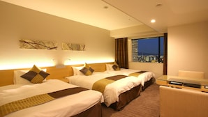 Quarto de hotel com duas camas, uma escrivaninha e vista para a cidade à noite.