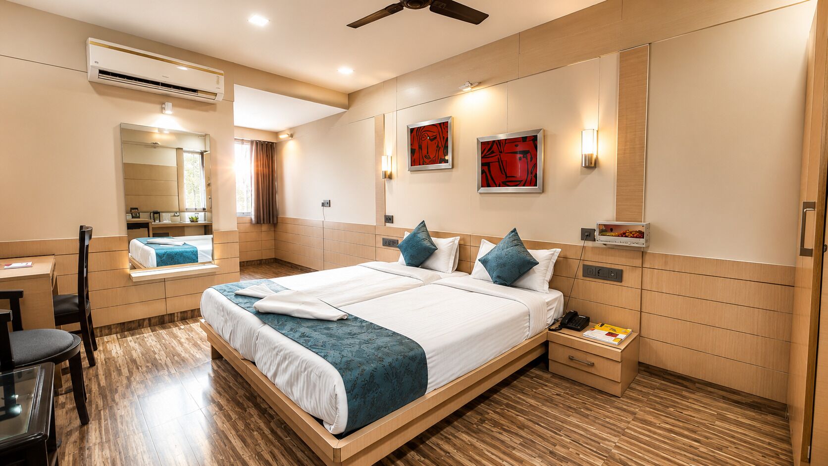 Quarto de hotel com uma cama grande, uma escrivaninha, uma cadeira, um espelho e obras de arte nas paredes.