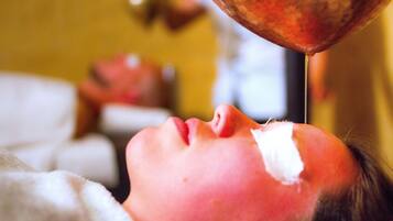 Uma pessoa deitada com um tecido branco no rosto, possivelmente recebendo um tratamento facial.