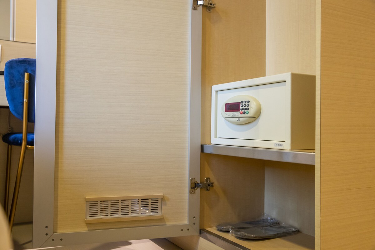 Quarto com um armário branco que contém um termostato digital, uma ventilação e um objeto embalado em plástico na prateleira inferior.