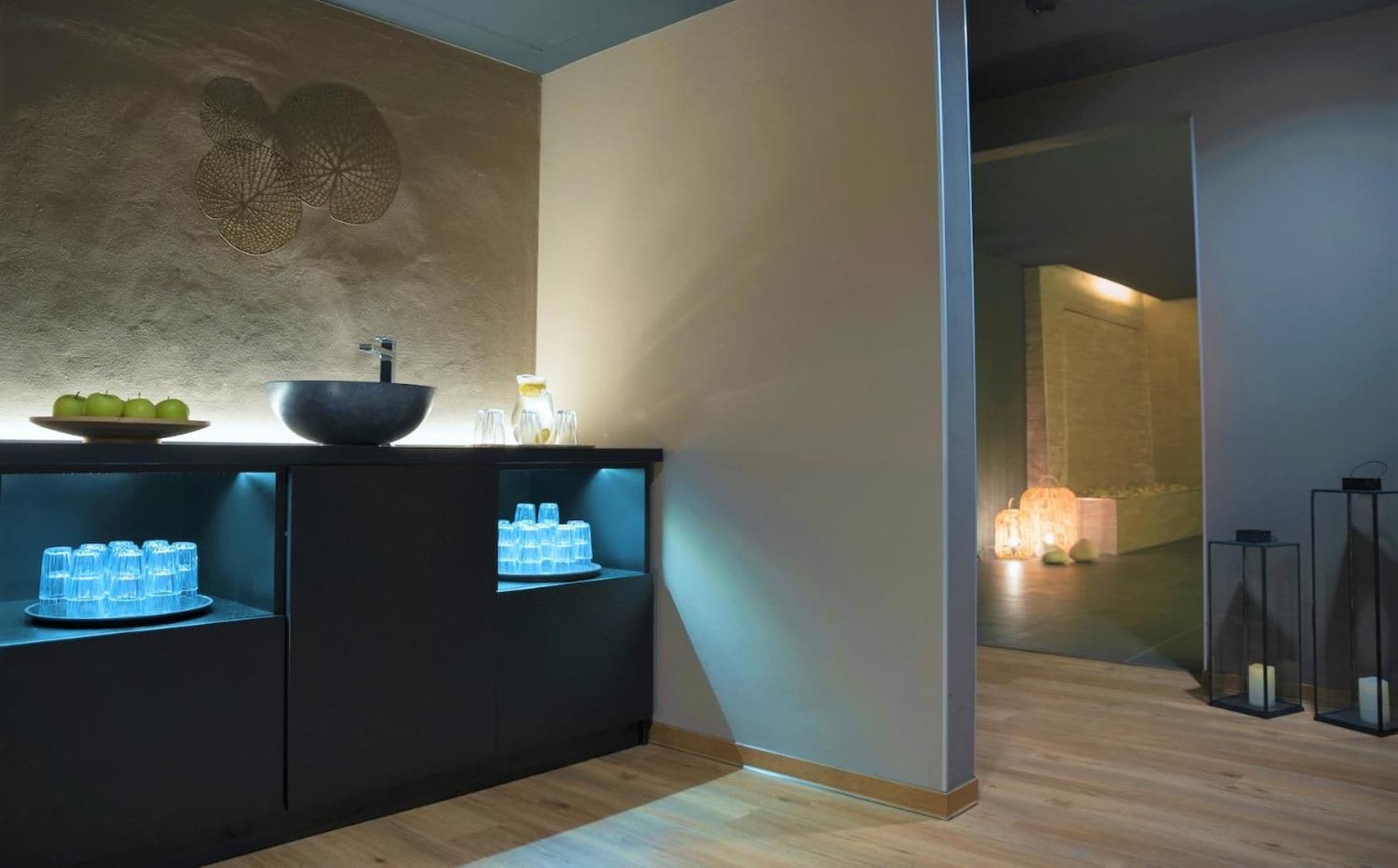 Interior moderno com console escuro exibindo uma tigela de maçãs, um jarro e copos.