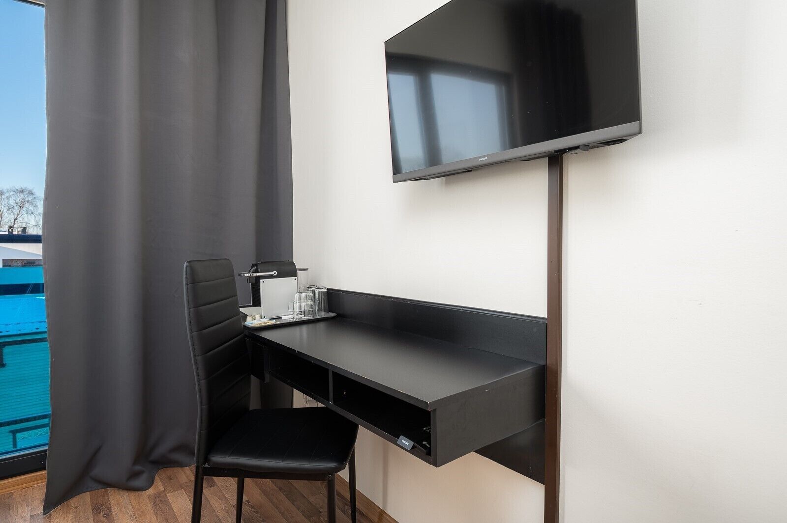 Quarto de canto com escrivaninha, cadeira e televisão de tela plana na parede.