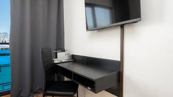 Quarto de canto com escrivaninha, cadeira e televisão de tela plana na parede.