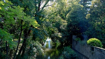 Um rio calmo com vegetação densa nas margens, uma ponte de pedra e uma cascata ao longe.