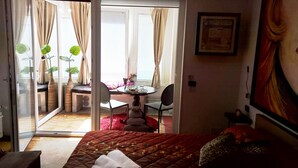 Quarto de hotel com cama, mesa de jantar com cadeiras, janela com cortinas e um quadro na parede.