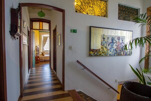 Um corredor com piso listrado, uma escada e um quadro na parede.