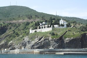 Um edifício costeiro com estrutura semelhante a uma igreja, rodeado por vegetação e um morro rochoso.