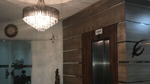 Um saguão com design de piso em formato de estrela, um candelabro, um elevador e uma estátua.