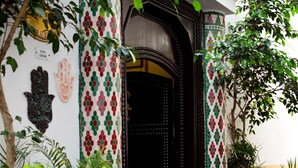 Entrada de edifício com porta decorativa, um ornamento de parede em formato de mão e plantas em vasos.