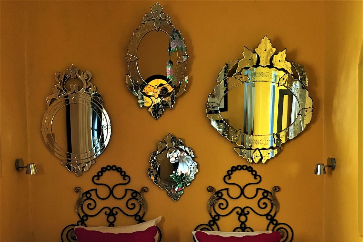 Quarto com duas camas, cada uma com cabeceira e almofadas. Quatro espelhos na parede, cada um com um design diferente.