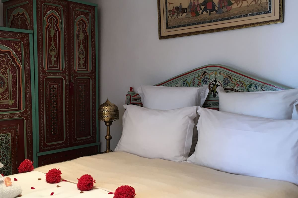 Quarto com cama, almofadas, cabeceira decorativa, guarda-roupa e um quadro pendurado na parede.