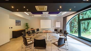 Uma sala de conferências com uma mesa grande, cadeiras, tela de projetor e um quadro branco.