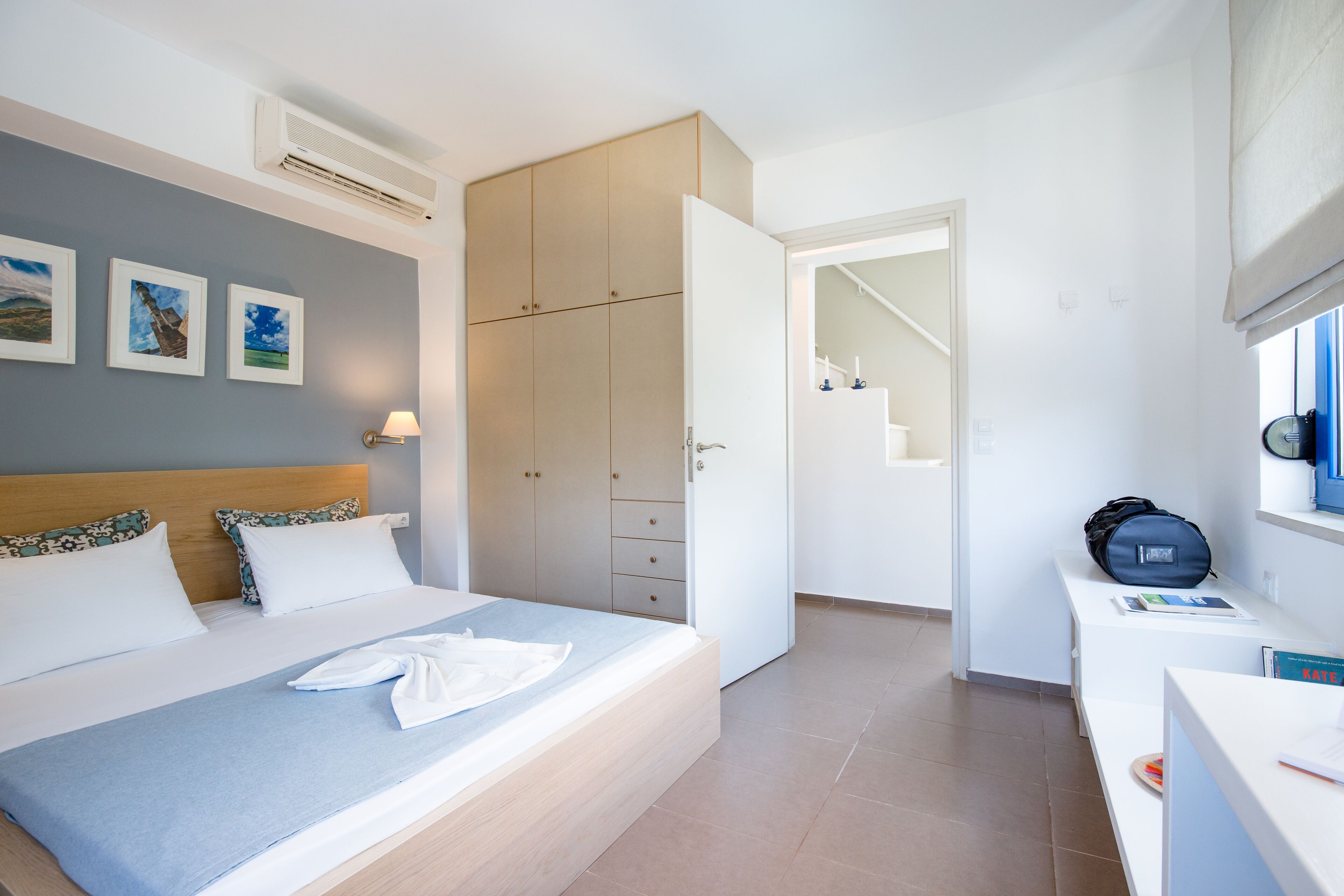 Quarto de hotel com cama, guarda-roupa, escrivaninha e escadas para o andar superior.