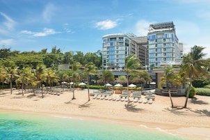 Um hotel à beira-mar com vários andares, praia de areia e palmeiras.