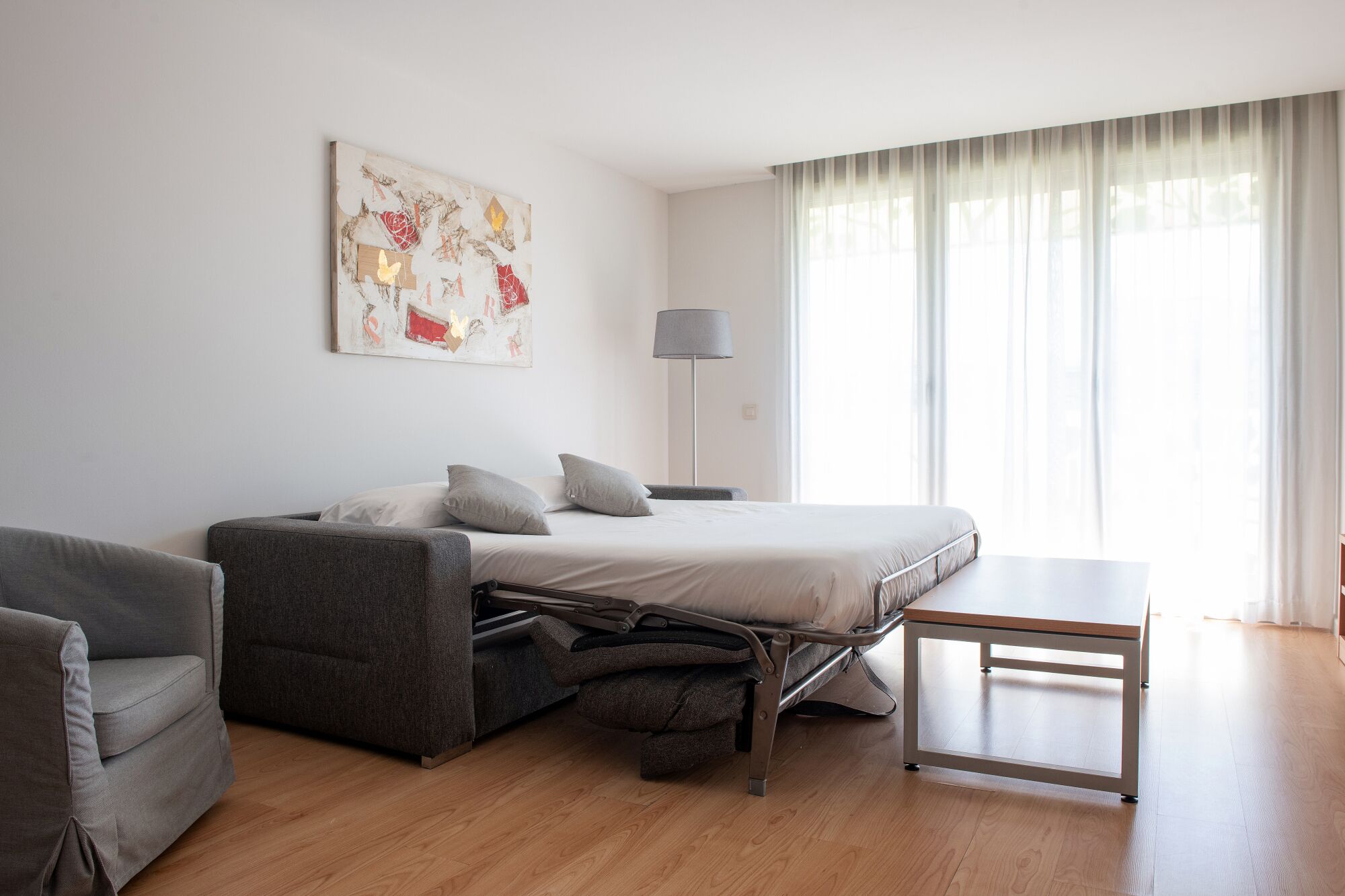 Quarto moderno com cama, sofá, mesa pequena e luminária.