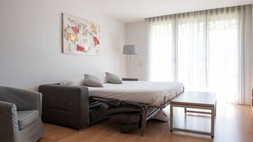 Quarto moderno com cama, sofá, mesa pequena e luminária.