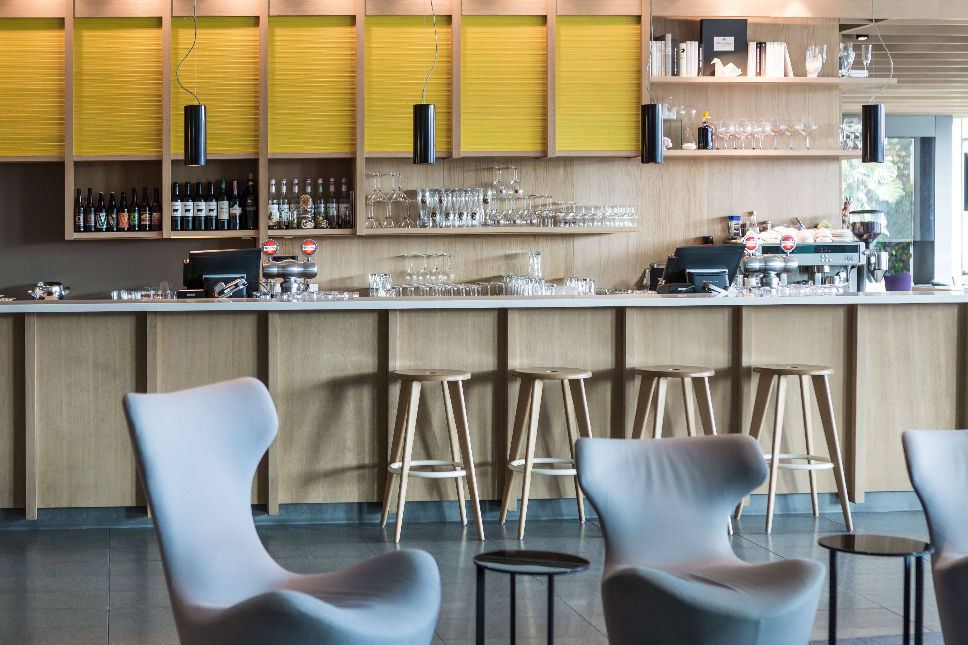 Uma área de bar moderna com balcão, banquetas e prateleiras com copos e garrafas.
