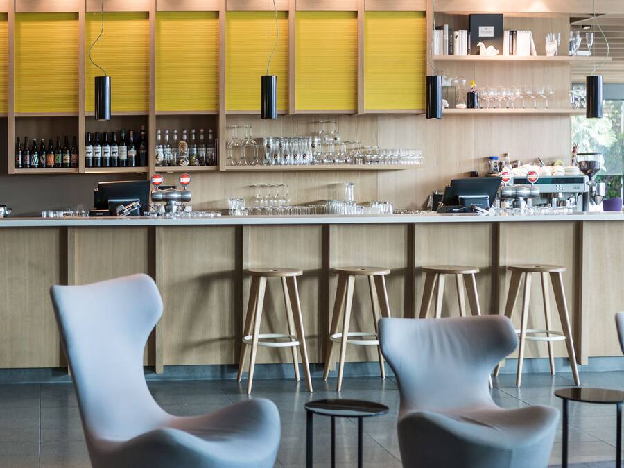 Uma área de bar moderna com balcão, banquetas e prateleiras com copos e garrafas.
